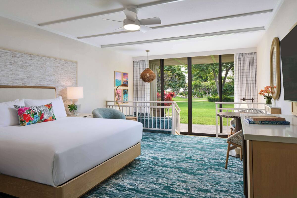 Quarto de hotel com cama, escrivaninha, cadeira e varanda com vista para o exterior.
