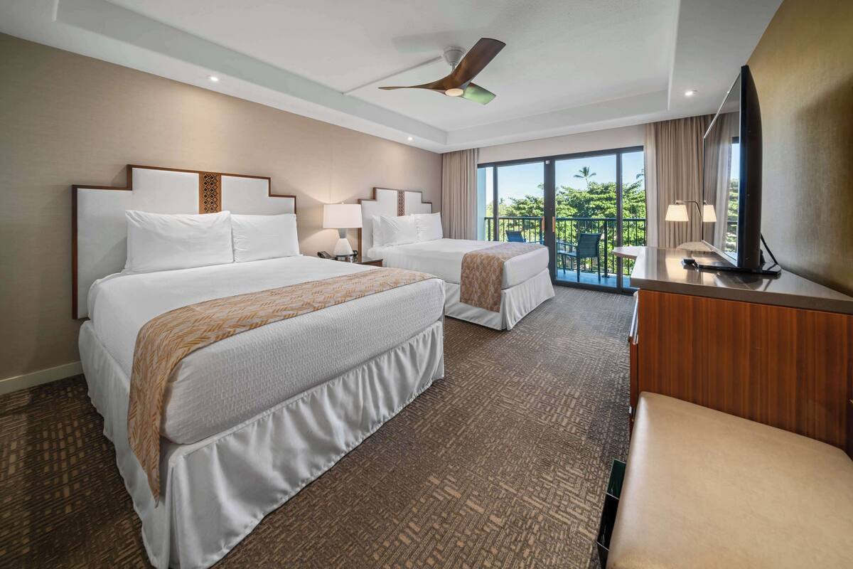 Quarto de hotel com duas camas, uma escrivaninha, uma cadeira, uma televisão e varanda com vista.