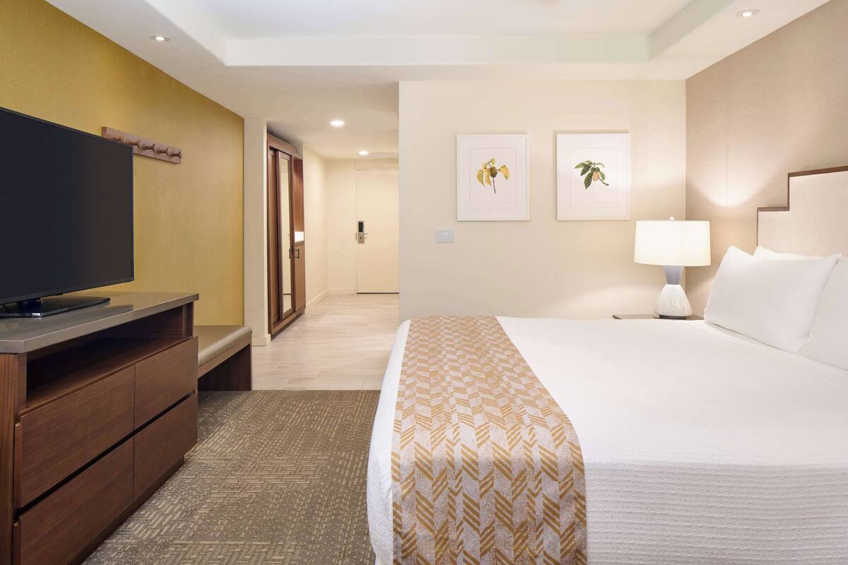 Quarto de hotel com cama, televisão, escrivaninha e obras de arte nas paredes.