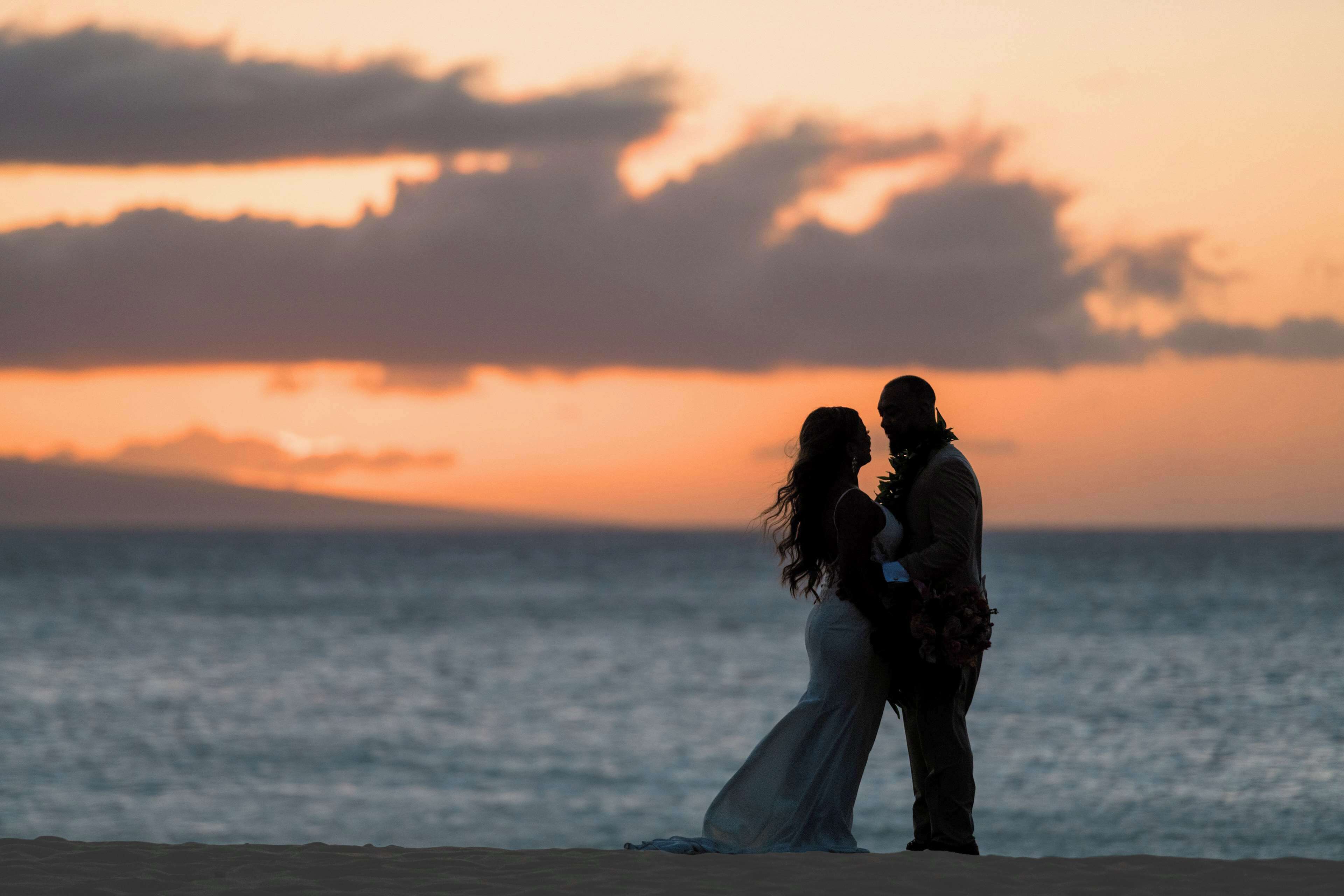 Um casal se abraçando ao pôr do sol à beira-mar.