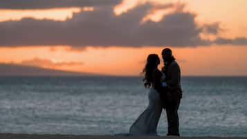 Um casal se abraçando ao pôr do sol à beira-mar.