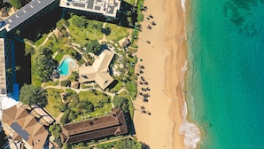 Vista aérea de um resort com praia, piscina e um edifício grande com painéis solares.