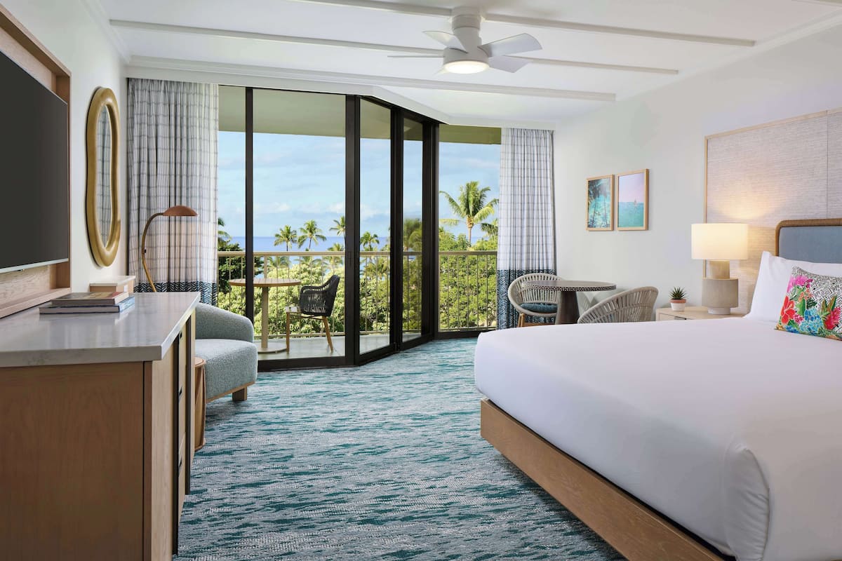 Quarto de hotel com cama, escrivaninha, cadeira, varanda e ventilador de teto.