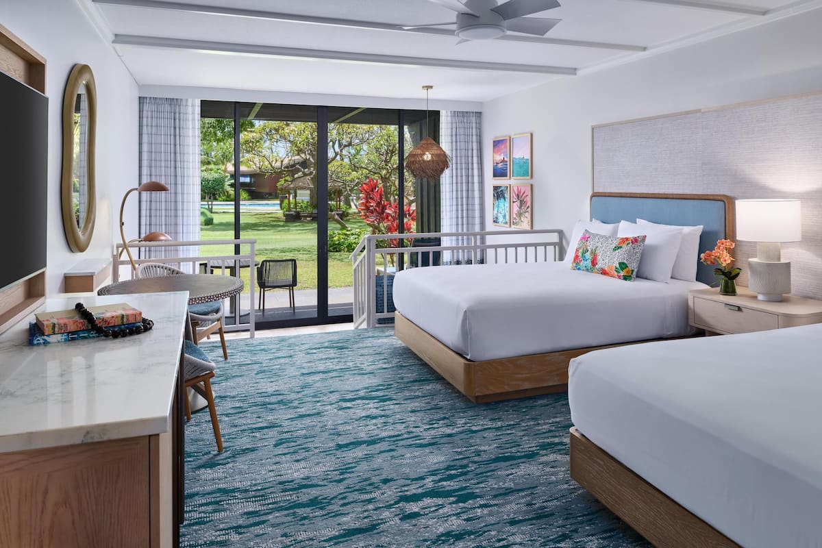 Quarto de hotel com cama, mesa de cabeceira, escrivaninha, cadeira e vista para um jardim através de janelas amplas.