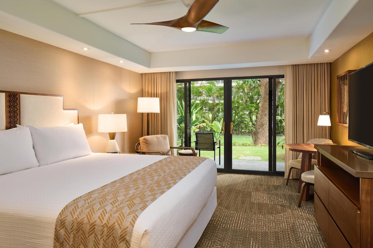 Quarto de hotel com uma cama grande, duas luminárias de cabeceira, uma escrivaninha com cadeira, televisão e vista para o exterior.