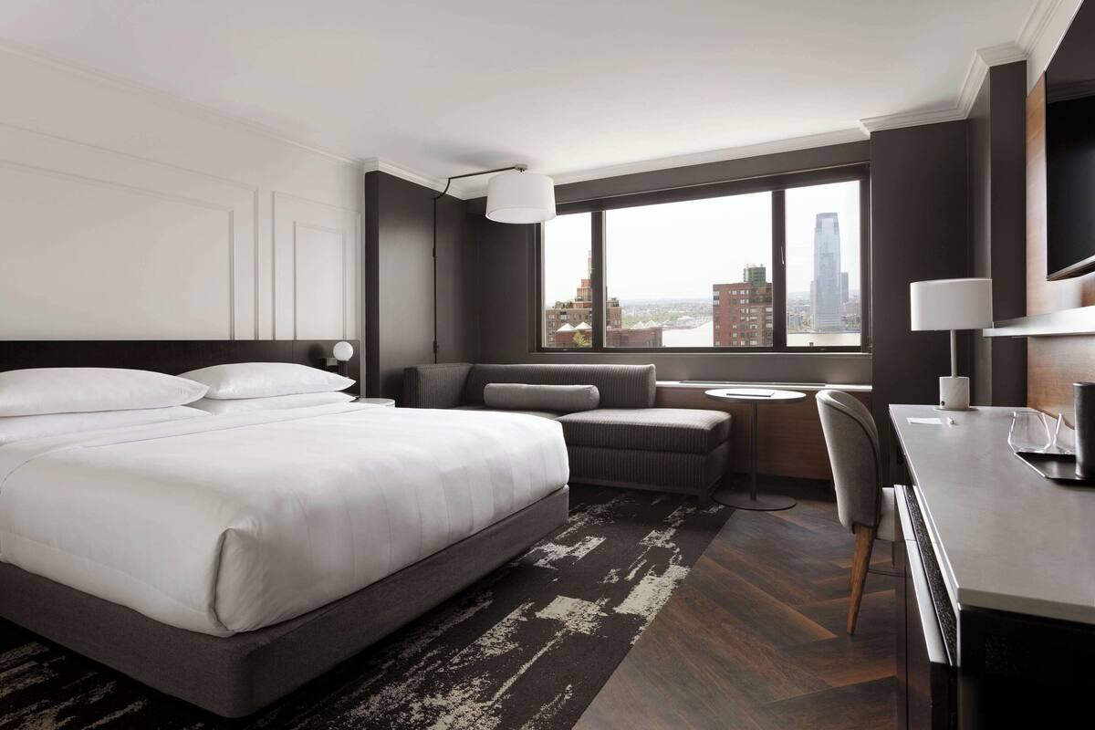 Quarto de hotel moderno com uma cama grande, um sofá, uma mesinha e uma televisão.