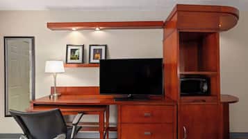 Quarto de hotel com escrivaninha de madeira, televisão, cadeira, luminária e micro-ondas.