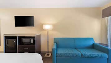 Quarto de hotel com cama, sofá azul, televisão de tela plana, micro-ondas e luminária de chão.