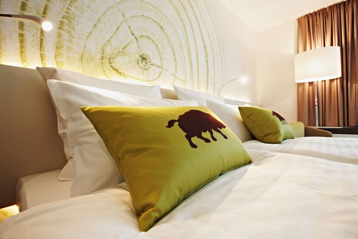 Quarto de hotel com cama, almofadas, luminária e parede com padrão circular.