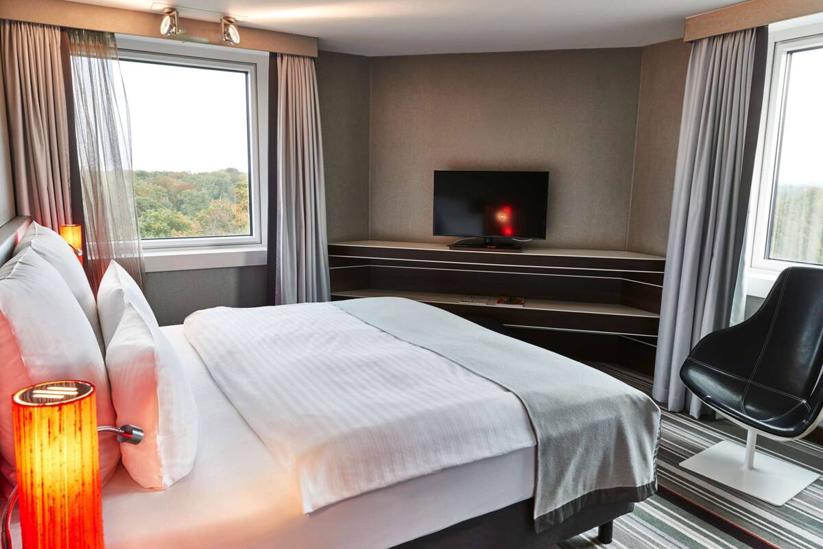 Quarto de hotel com cama, televisão, escrivaninha e cadeira.