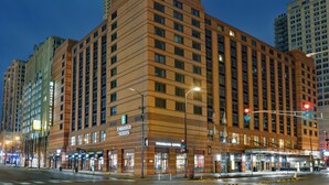 Um hotel com vários andares, um letreiro chamativo da 'Embassy Suites', uma cafeteria Starbucks e uma rua bem iluminada à noite.