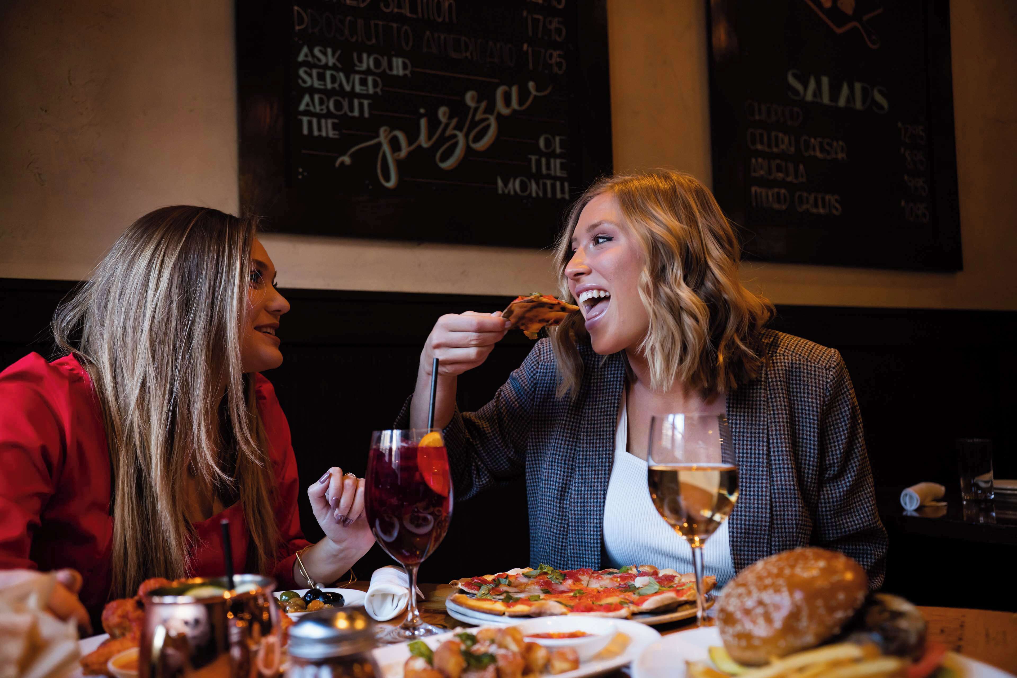 Duas pessoas jantando em um restaurante, com pizza e bebidas na mesa.