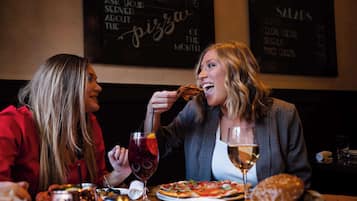 Duas pessoas jantando em um restaurante, com pizza e bebidas na mesa.