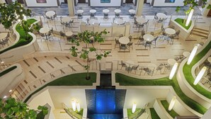 Um espaço interior em vários níveis, com uma fonte central, rodeado por zonas de estar e vegetação.
