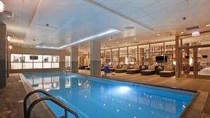 Uma piscina com parede de vidro, área de estar com sofás e uma placa de saída.