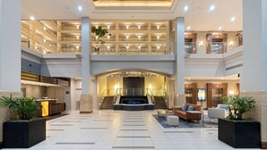 Um hall amplo com escadaria central, vários andares, balcão de recepção e áreas de estar.