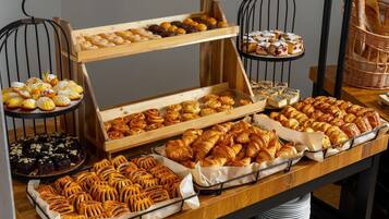 Mesa de buffet com diversos produtos de panificação, incluindo doces e pão, dispostos em tábuas e bandejas de madeira.