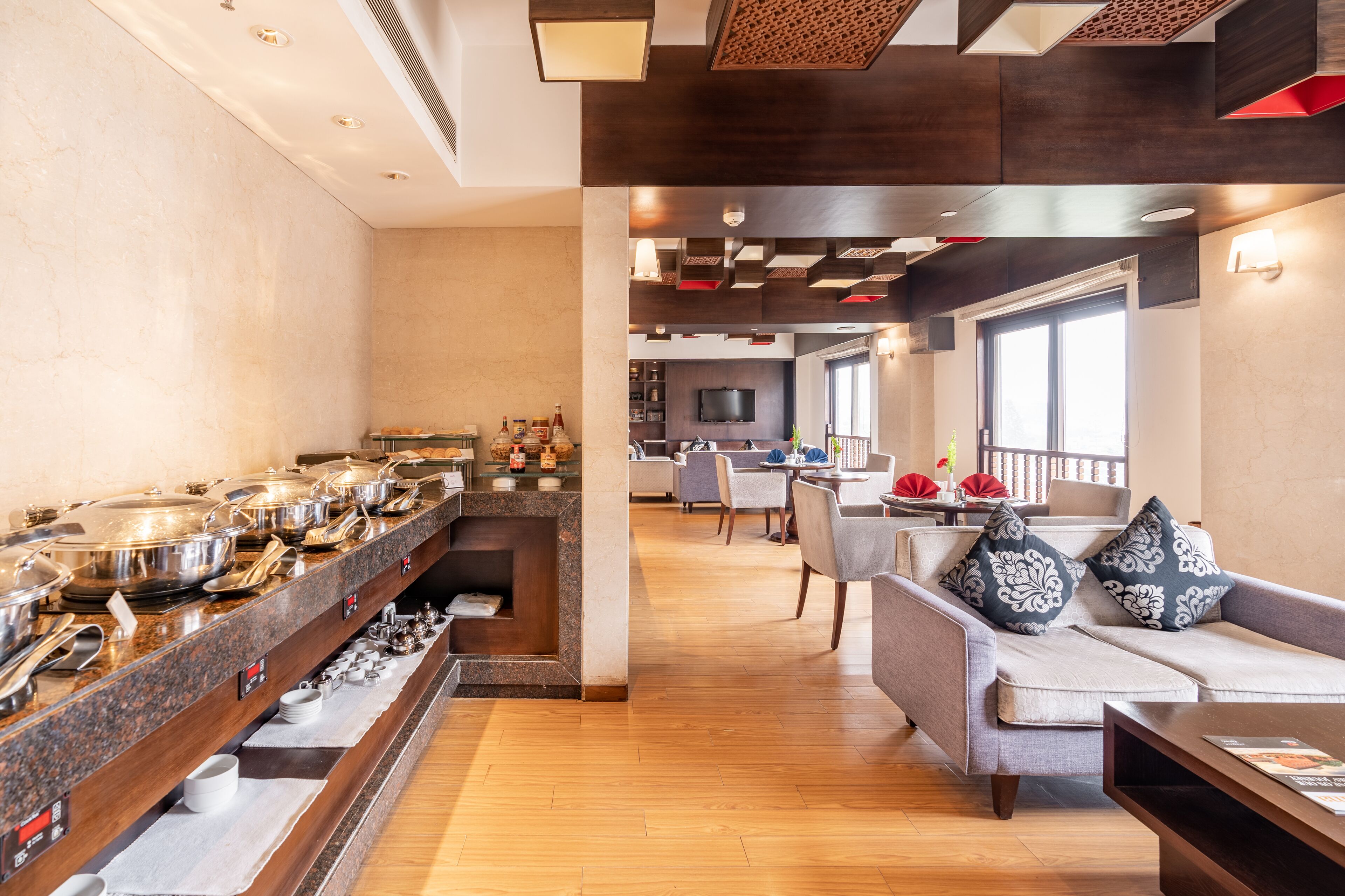 Um lobby moderno de hotel com área de buffet, assentos e televisão.