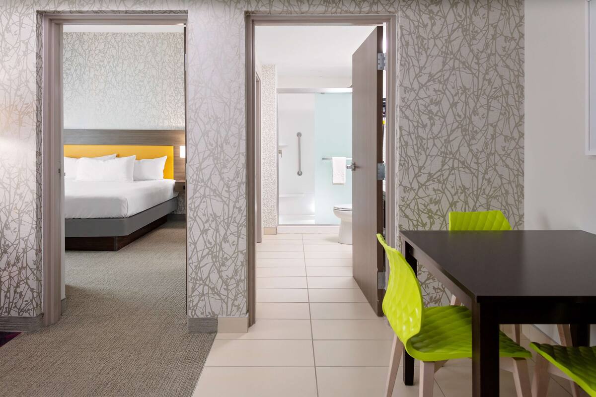 Quarto de hotel com cama, banheiro e área de jantar com cadeiras.