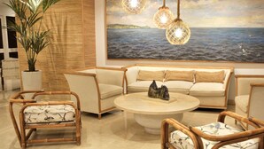 Uma sala de estar moderna com uma grande pintura de paisagem marítima, uma mesa de centro redonda e móveis de vime.