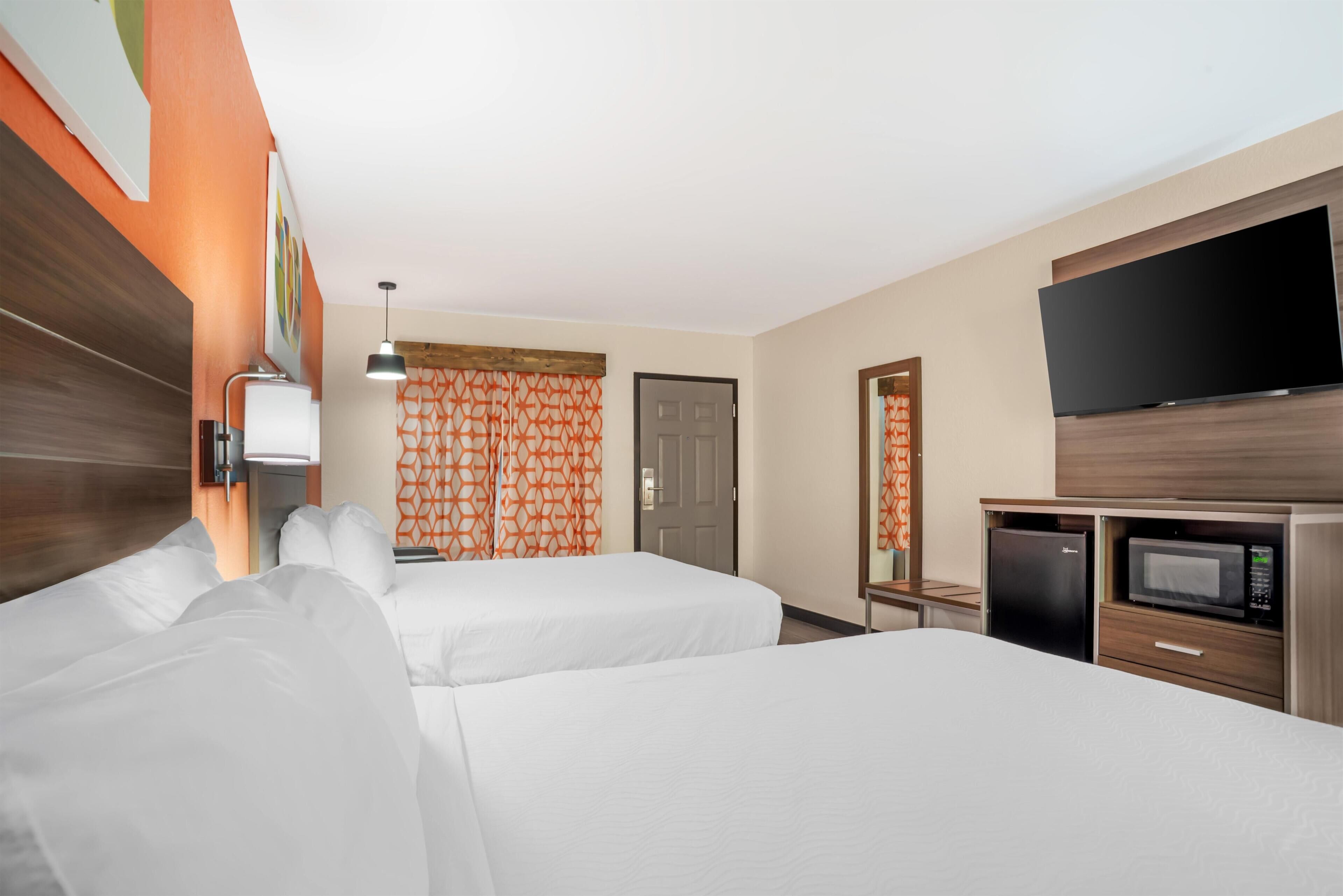 Quarto de hotel com duas camas, televisão de tela plana, micro-ondas e geladeira.