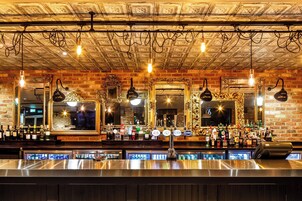 Um bar com vários espelhos, uma parede de tijolos e uma variedade de garrafas e copos.