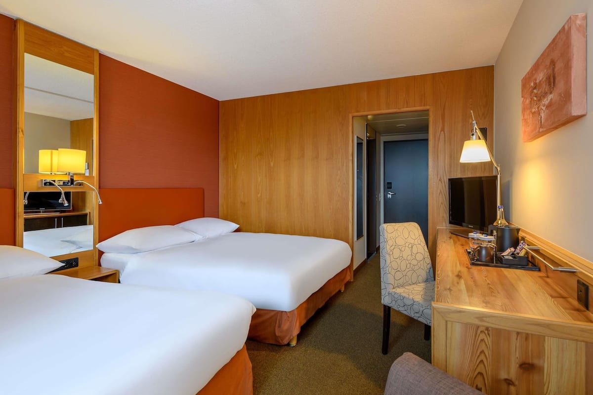Quarto de hotel com duas camas, uma escrivaninha com abajur, uma cadeira, televisão e espelho.