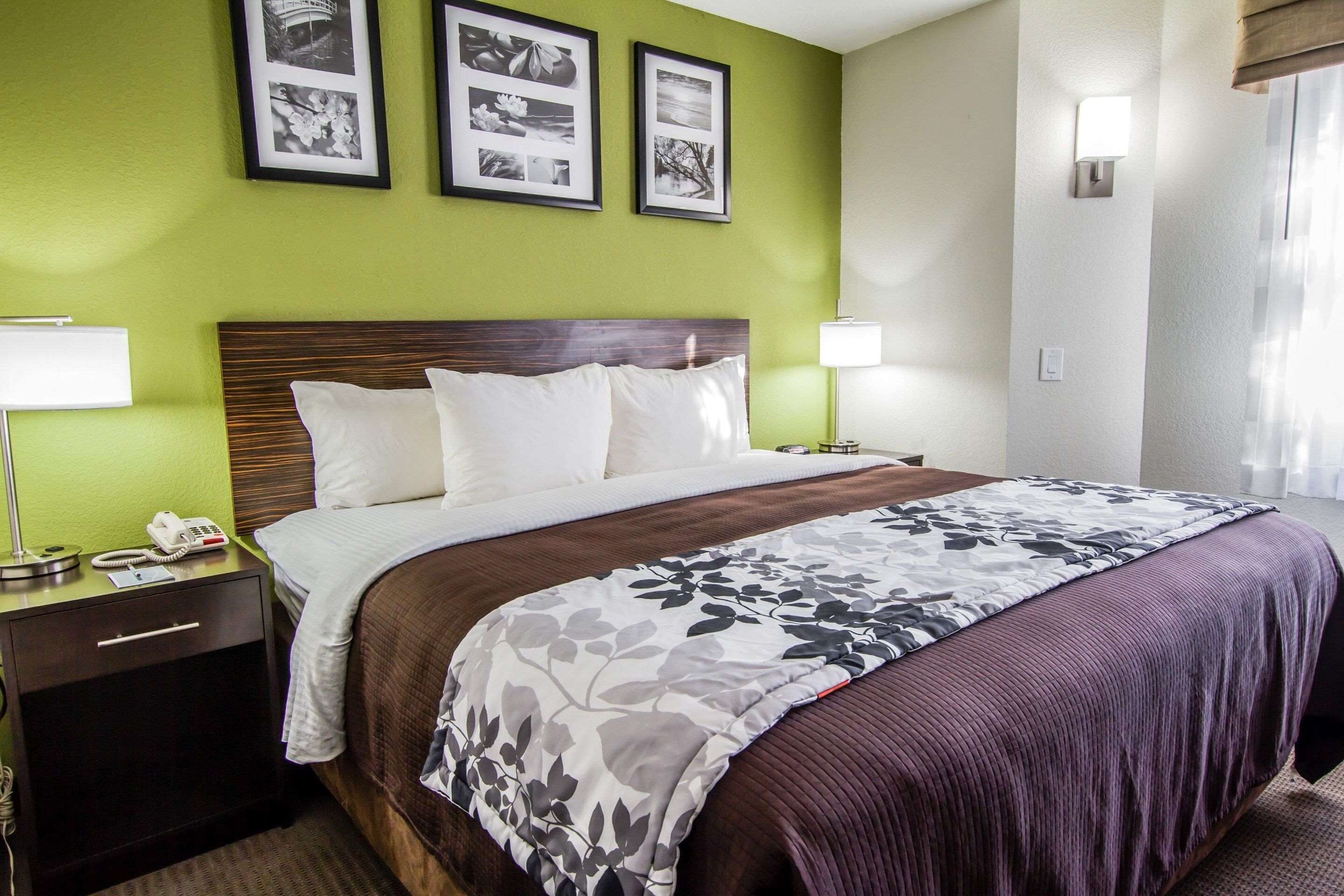 Quarto de hotel com uma cama grande, duas mesinhas de cabeceira com abajures, um telefone e quadros nas paredes.