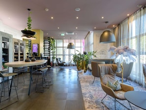 Um saguão de hotel moderno com área de bar, assentos e janelas amplas.