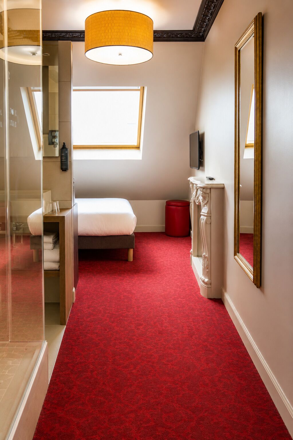 Quarto de hotel com carpete vermelho, uma cama, televisão, espelho e janela.