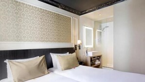 Quarto de hotel com uma cama grande, mesa de cabeceira, espelho e área de chuveiro.