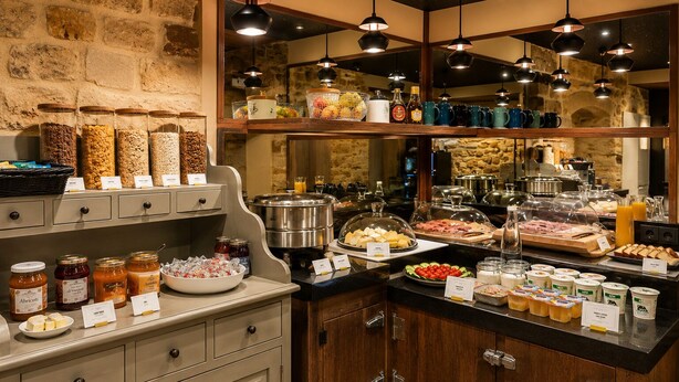 Um buffet de café da manhã com diversos alimentos, potes de condimentos e um fundo de parede de pedra.