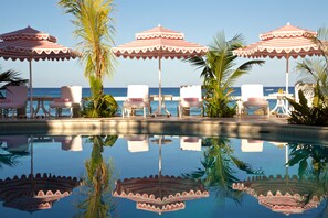 Área da piscina com espreguiçadeiras e guarda-sóis listrados, refletindo na água.