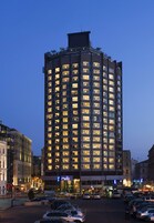 Um hotel moderno com muitos andares, janelas iluminadas e uma entrada central.