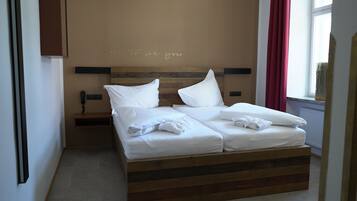 Cama bem arrumada com roupa de cama e almofadas brancas, cabeceira de madeira e mesa de cabeceira com abajur.