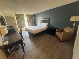 Quarto de hotel com cama, escrivaninha, cadeira e luminária.
