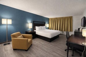 Quarto de hotel com cama, escrivaninha, cadeira e abajur.