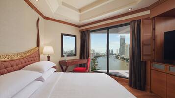 Quarto de hotel com uma cama grande, uma escrivaninha, uma cadeira, uma televisão e vista para a cidade e o rio.