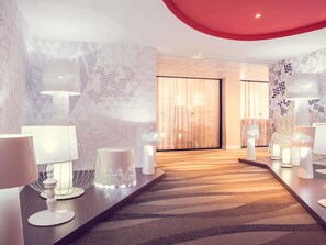 Um hall de hotel moderno com um caminho central, padrões decorativos na parede e iluminação ambiente.