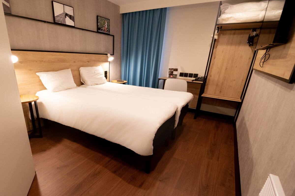 Quarto de hotel moderno com uma cama grande, mesas de cabeceira, uma escrivaninha e um guarda-roupa.