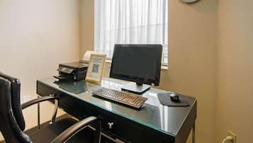 Um escritório pequeno com uma mesa, computador, teclado, rato, cadeira e um relógio na parede.