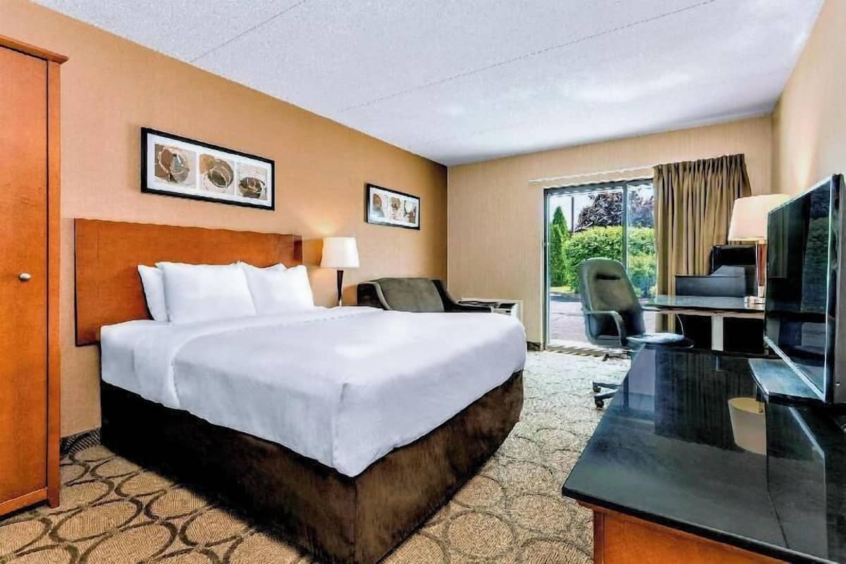 Quarto de hotel com cama, escrivaninha com computador, cadeira e televisão.