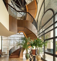 Um interior com vários níveis, uma escadaria em espiral, grandes janelas e plantas dentro de casa.
