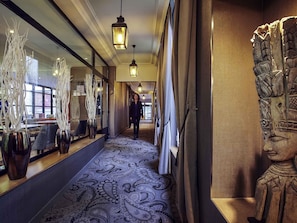 Corredor de hotel com carpete estampado, luminárias pendentes e uma grande estátua.