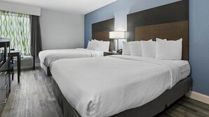 Quarto de hotel com duas camas, uma escrivaninha e uma luminária.