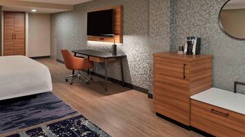 Quarto de hotel com cama, escrivaninha, cadeira, cômoda, cafeteira e espelho.