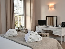 Quarto de hotel com cama, escrivaninha com computador, luminária e janela com cortinas.