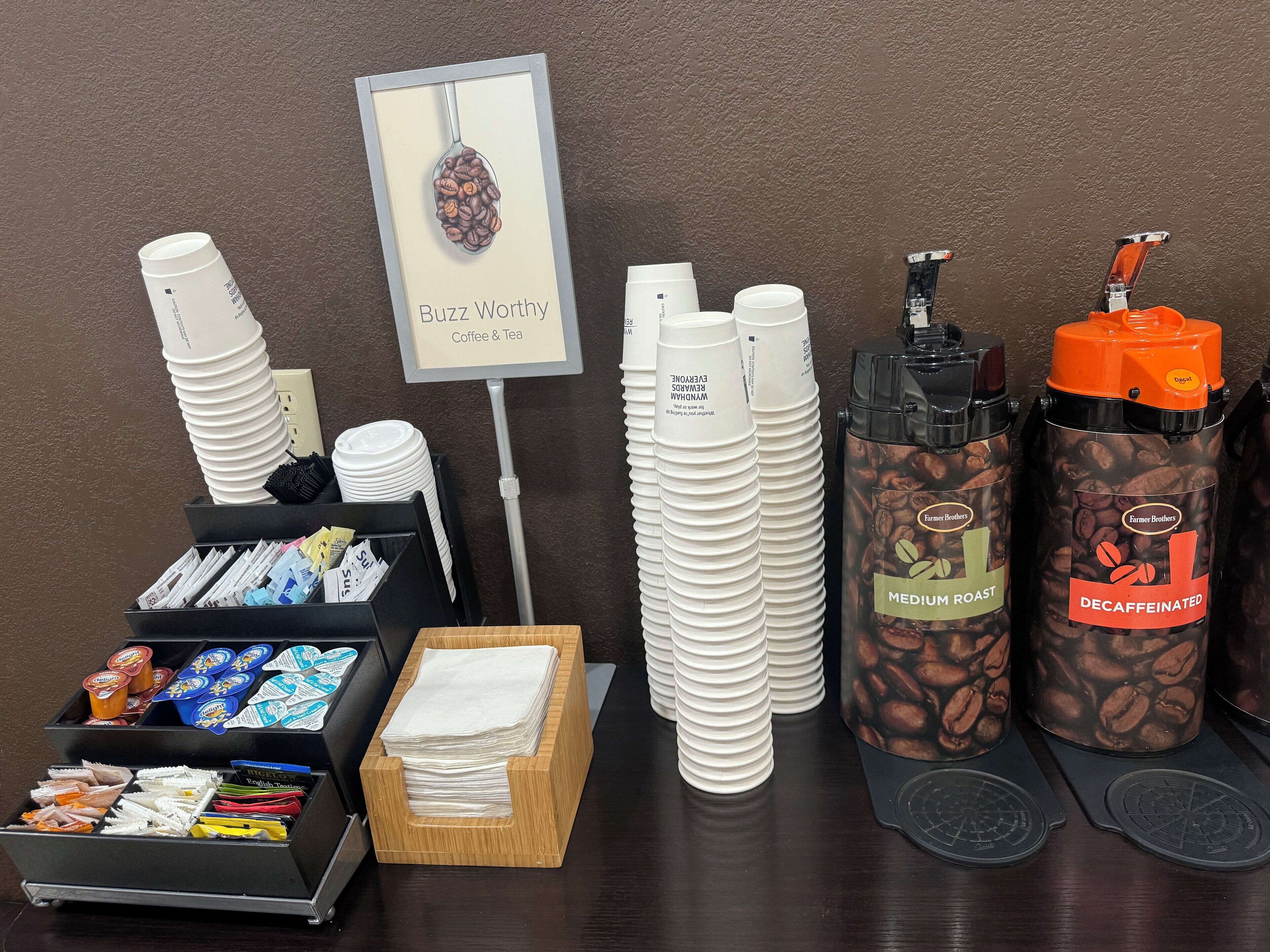 Cantinho de café com copos descartáveis, grãos de café e um letreiro com a inscrição 