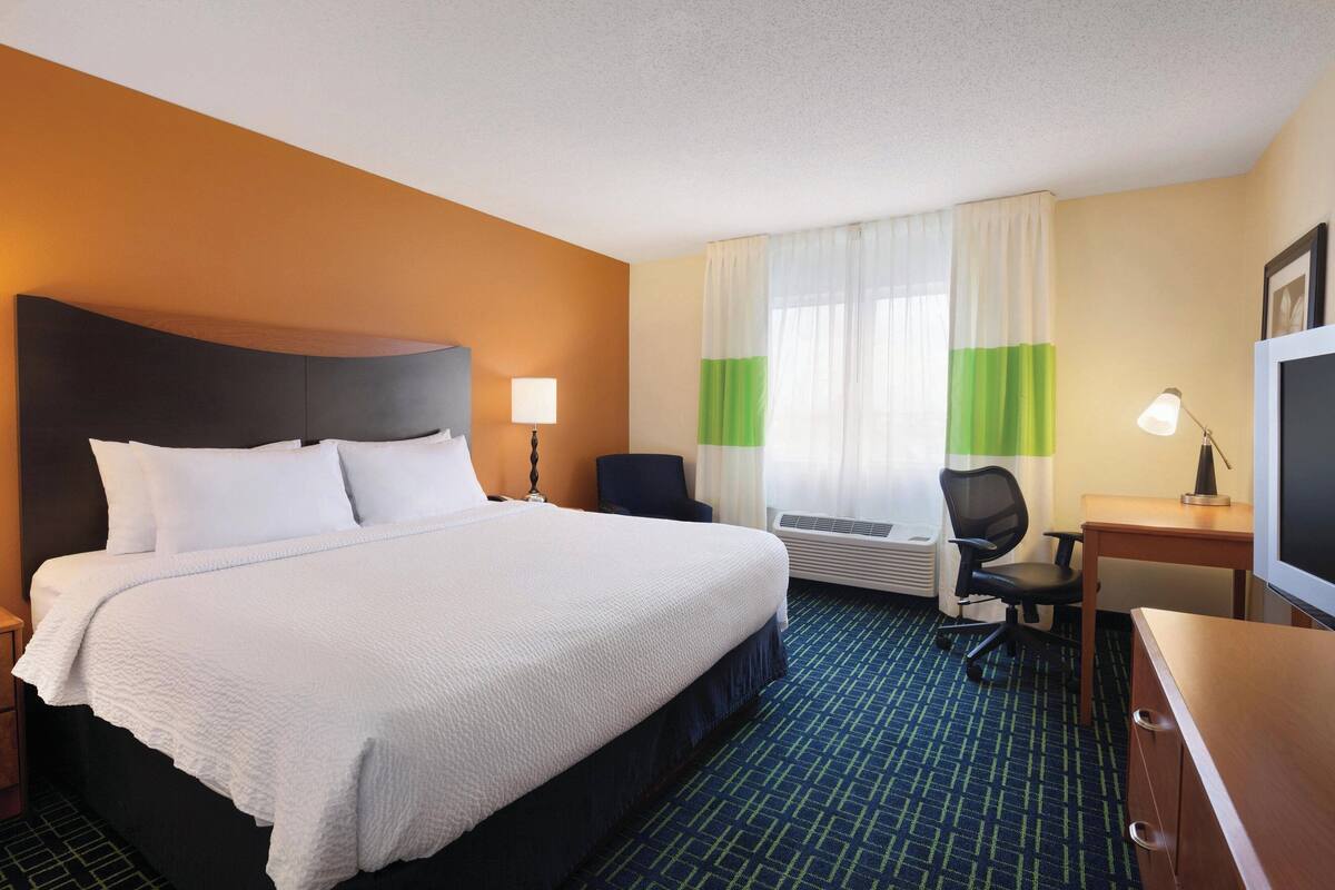 Quarto de hotel com uma cama grande, uma escrivaninha, uma cadeira e uma televisão.