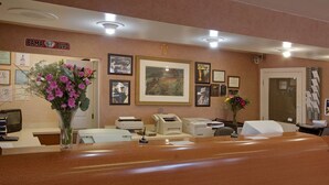Uma área de recepção com balcão de madeira, quadros nas paredes, uma cruz e uma placa com a inscrição 'BAMA BLVD'.